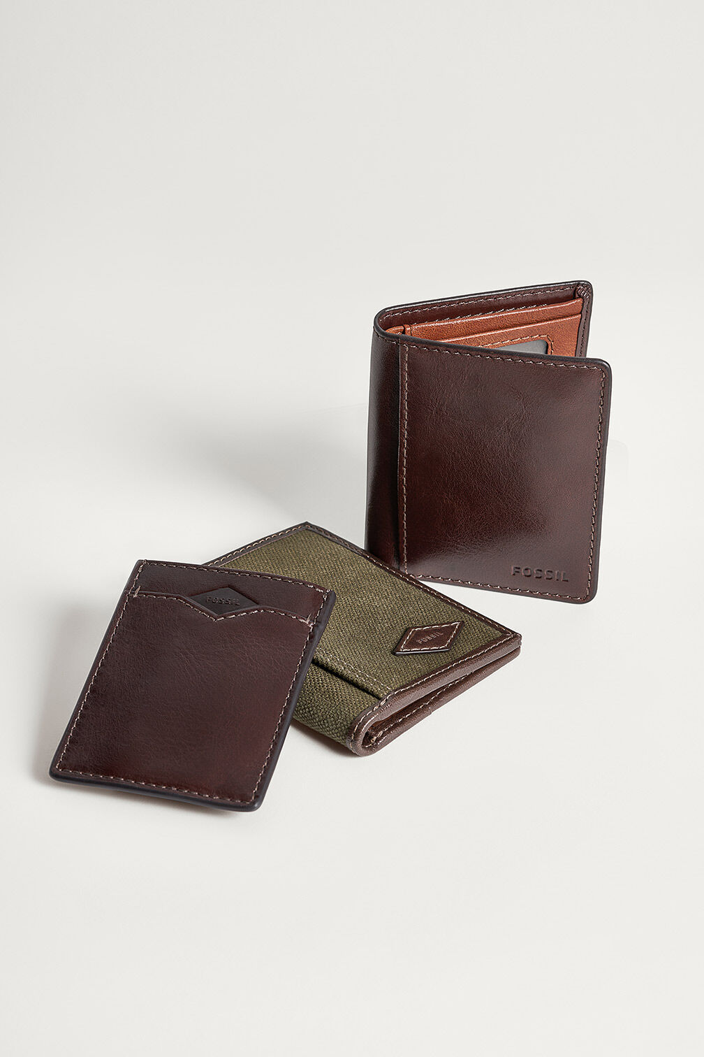 A group shot of three Fossil men's wallets in brown and green colorways.